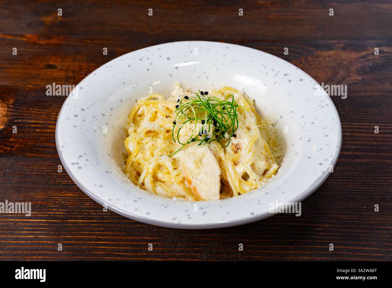 A bowl of creamy pasta topped with delicate herbs sits on a wooden ...