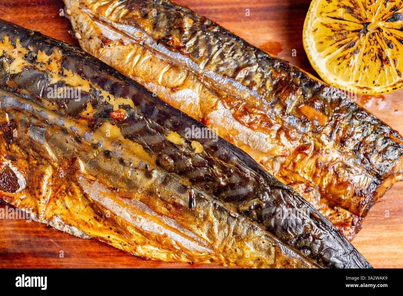 Two grilled mackerel fillets are placed on a wooden board. Accompanying ...