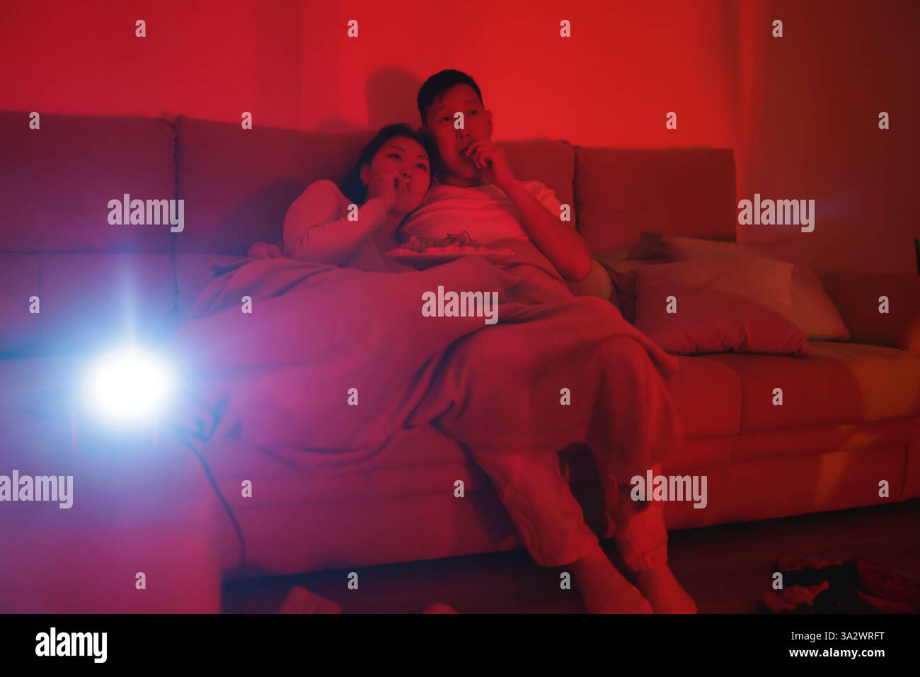 Young couple watching movie using projector at home and eating snacks ...