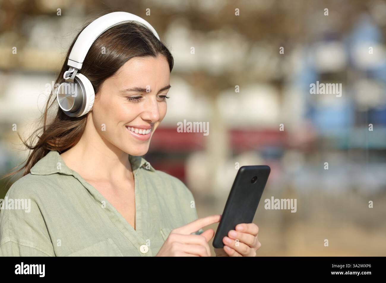 Happy woman wearing headphone using mobile phone in the street Stock ...