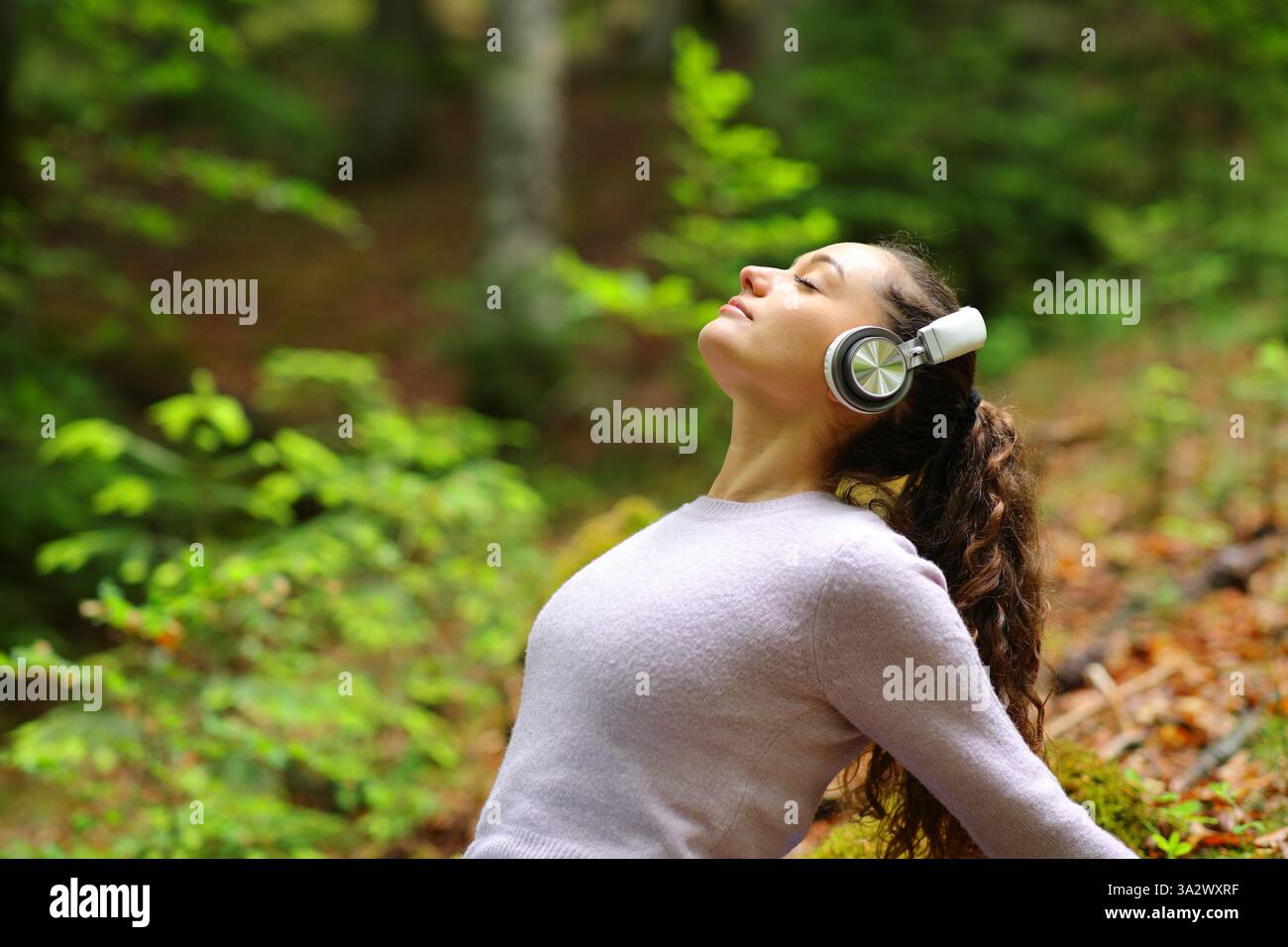 Profile of a woman relaxing in a forest listening audio with headphone ...