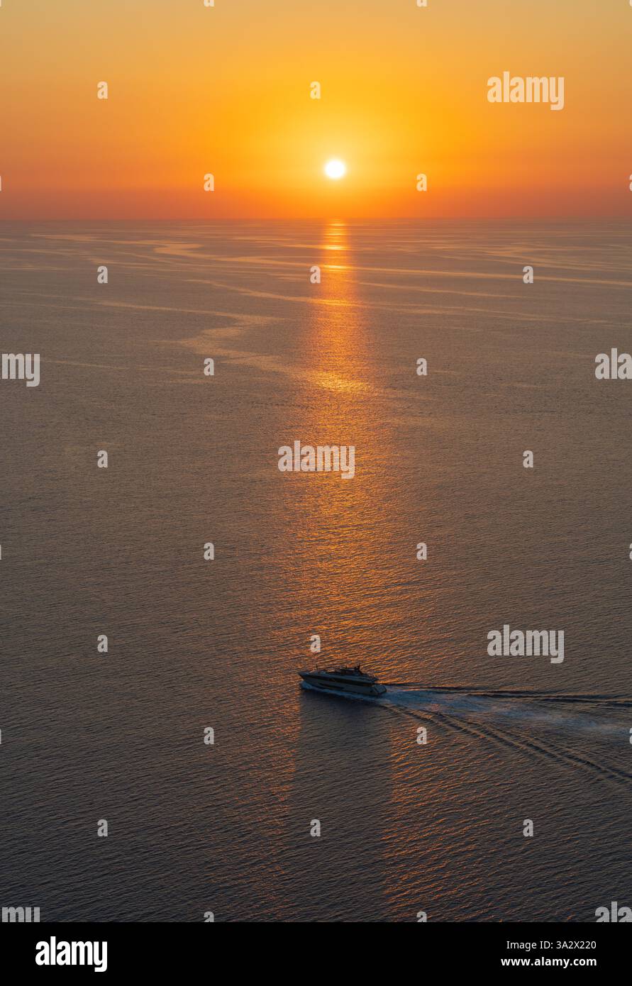 Tourist ship sails on calm sea in sunset sea light. Yellow-orange sky ...