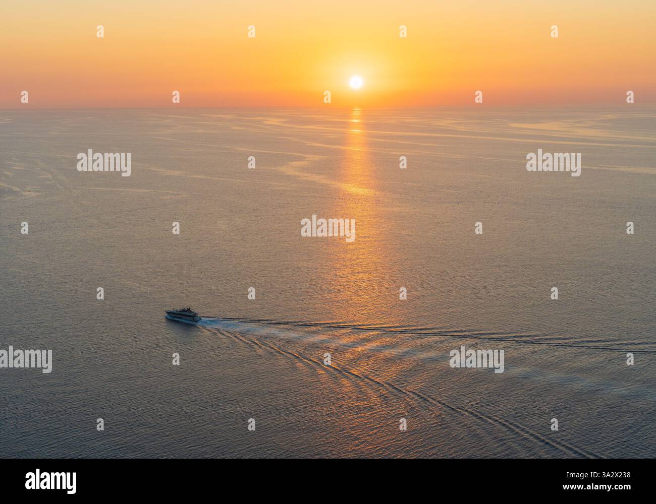 Tourist ship sails on calm sea in sunset sea light. Yellow-orange sky ...