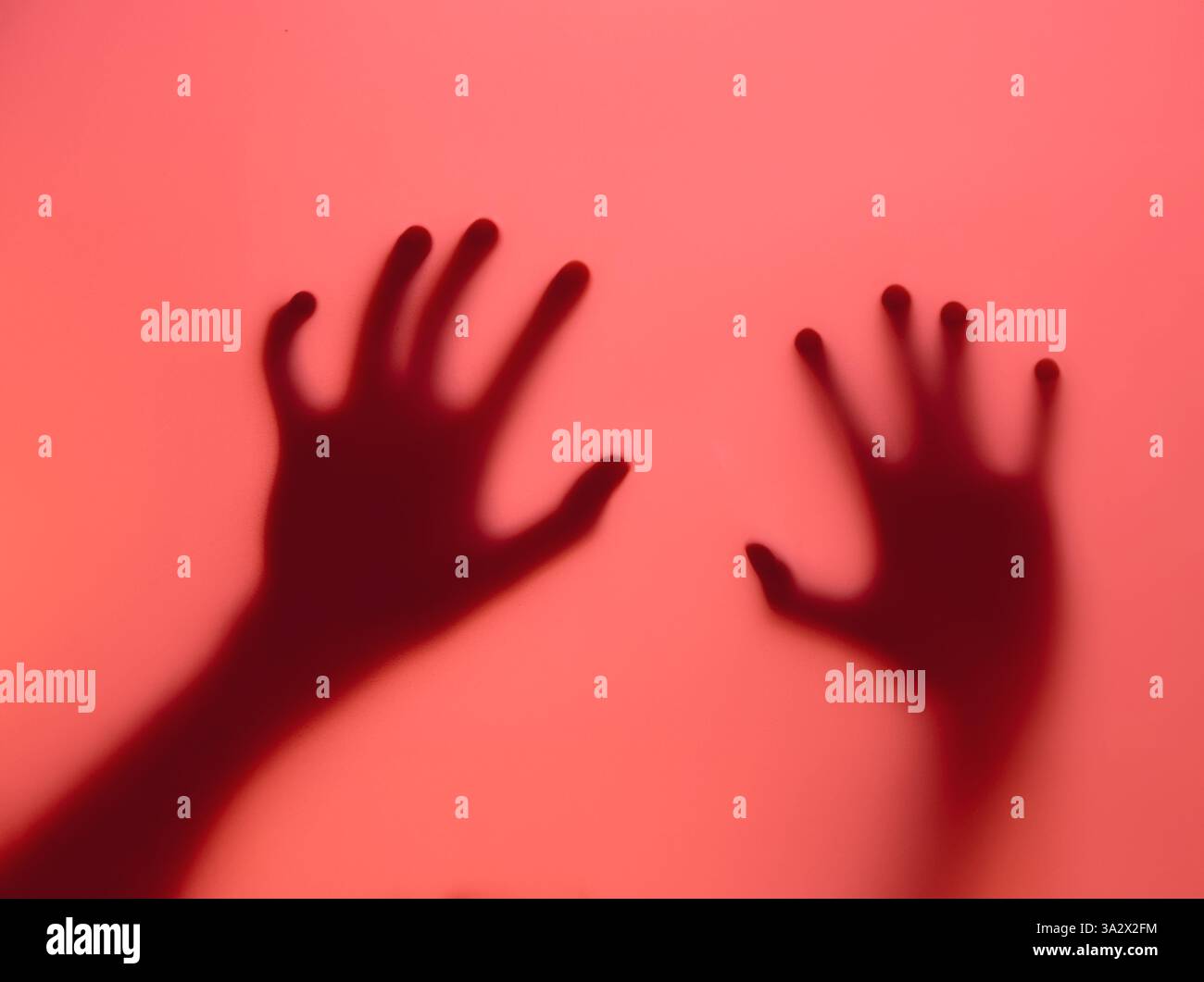 Shadowy forms of two hands are seen silhouetted against a textured red ...