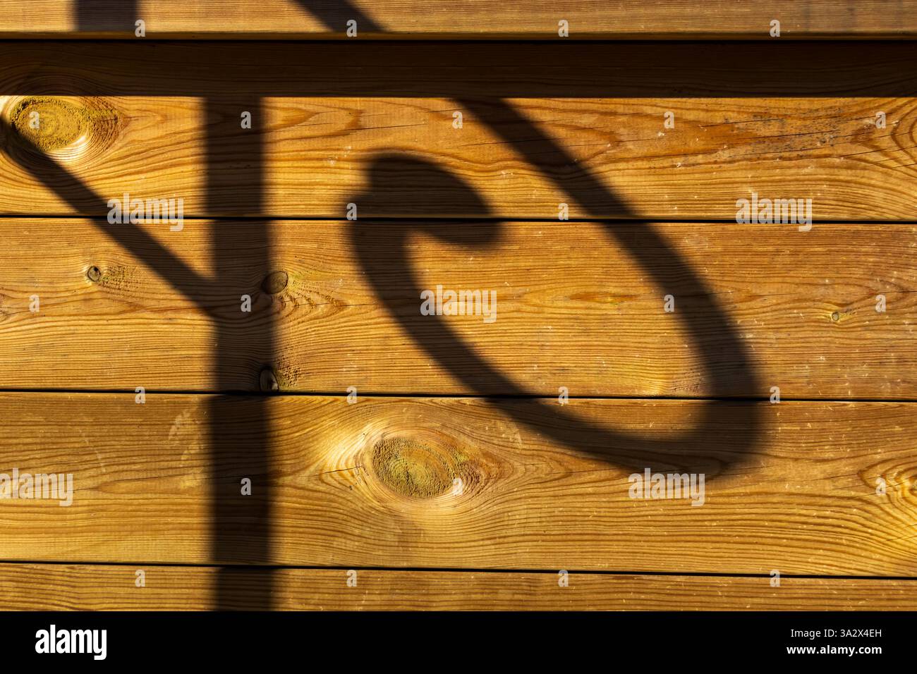 A shadow of a coiled rail falls across an outdoor wooden plank wall ...