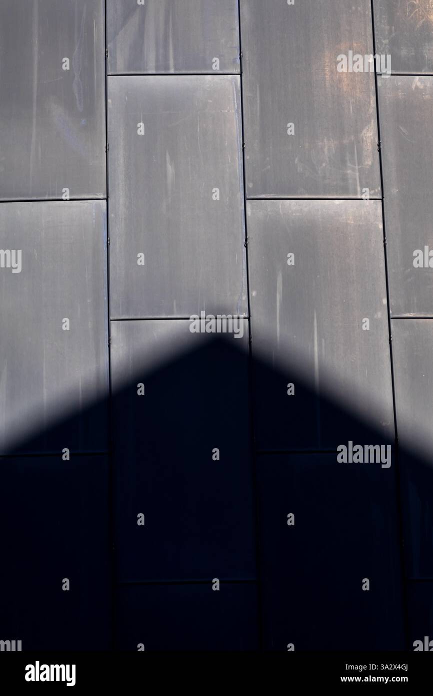 A sharp triangular roof shadow cuts across the rectangular metal facade ...