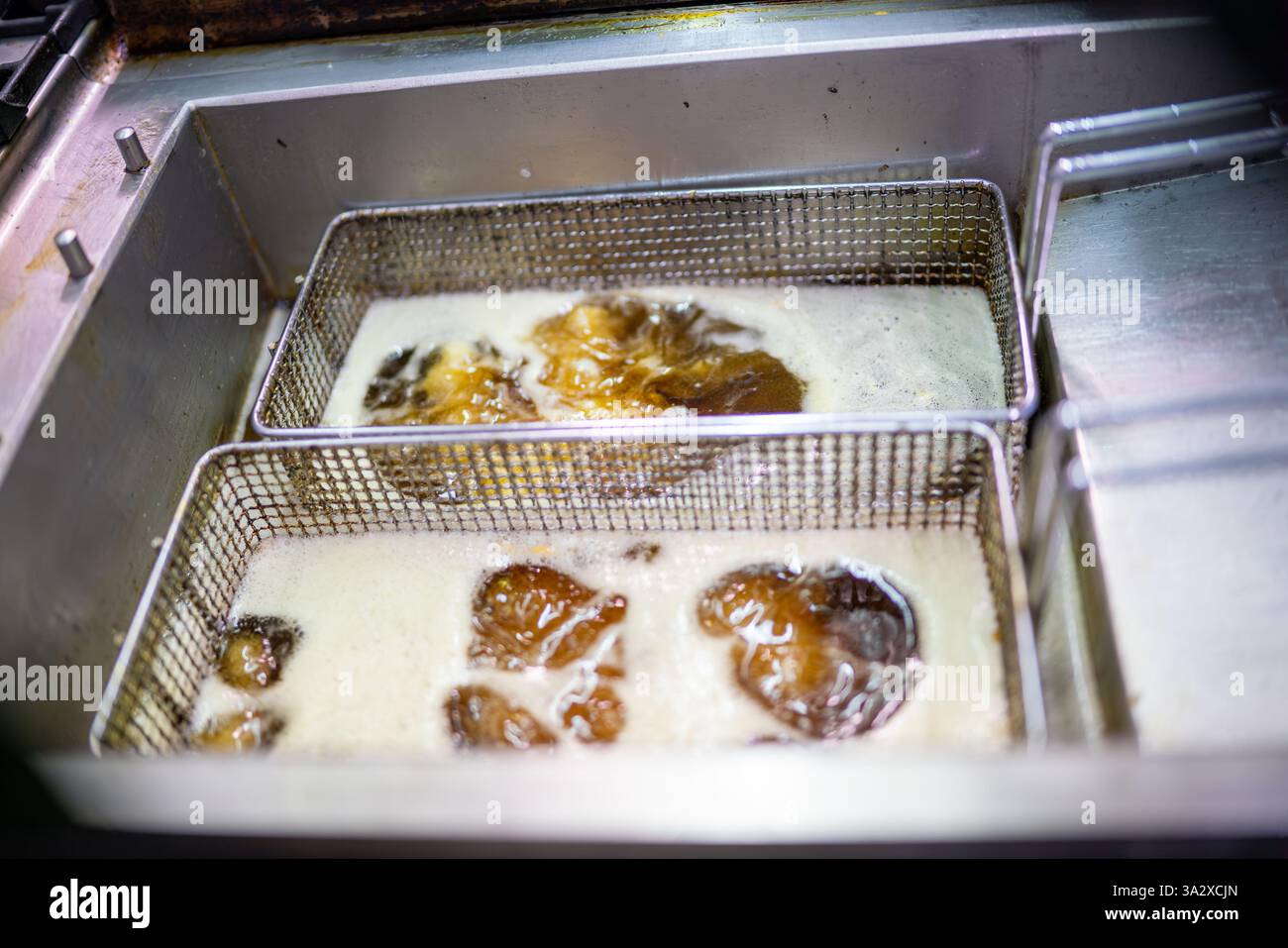 Metal basket lifting crispy fried food from bubbling oil inside a deep ...
