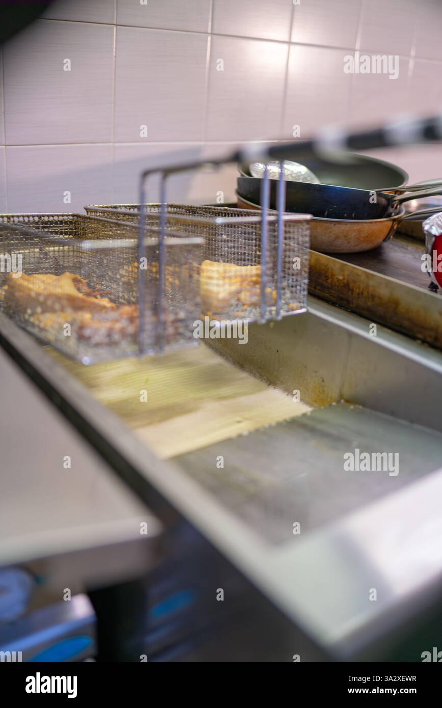 Metal fry baskets filled with samosas dripping oil into a deep fryer in ...