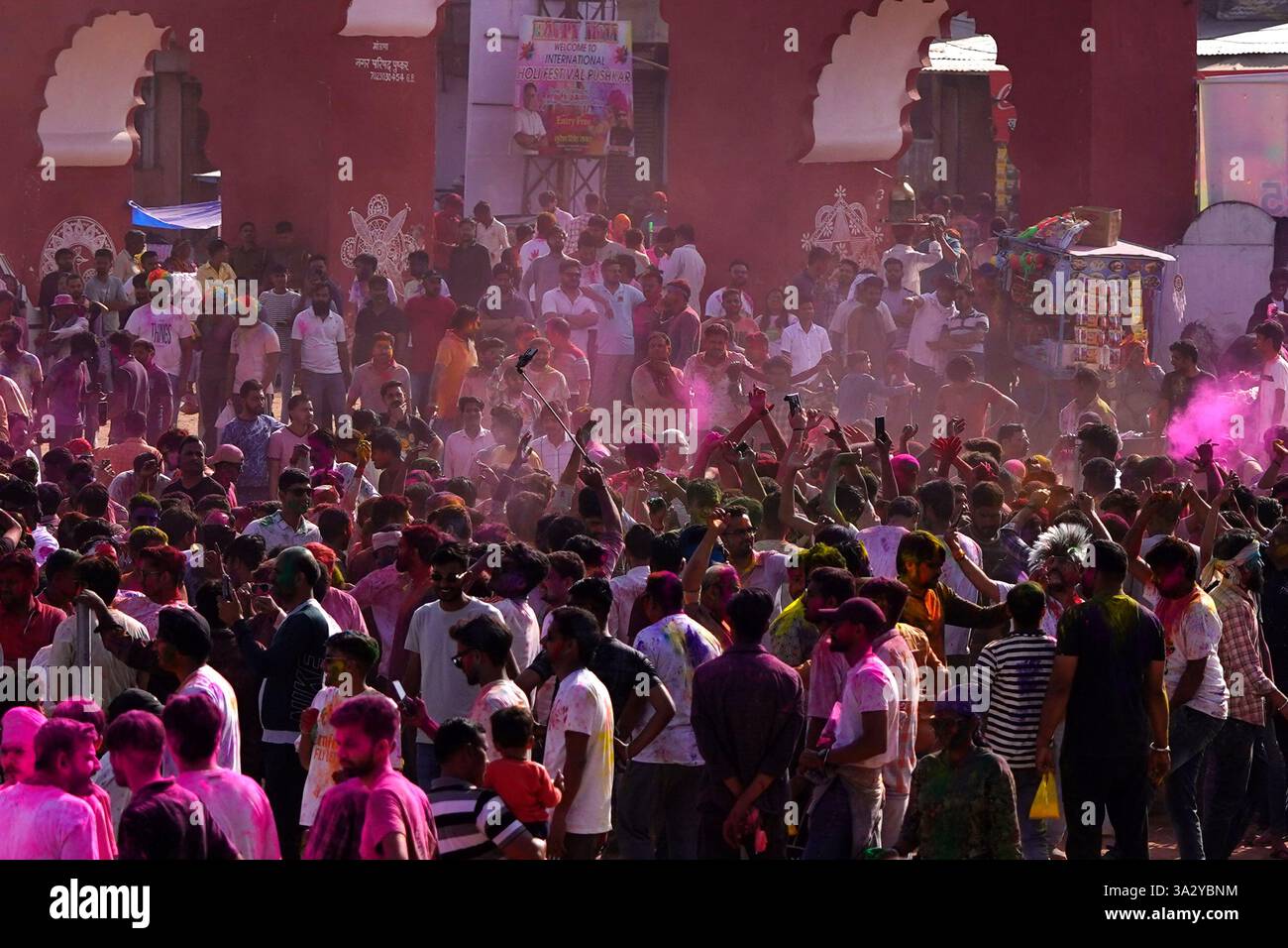 Pushkar, India. 14th Mar, 2025. Indian people dance as they throw colored powder and spray water ...