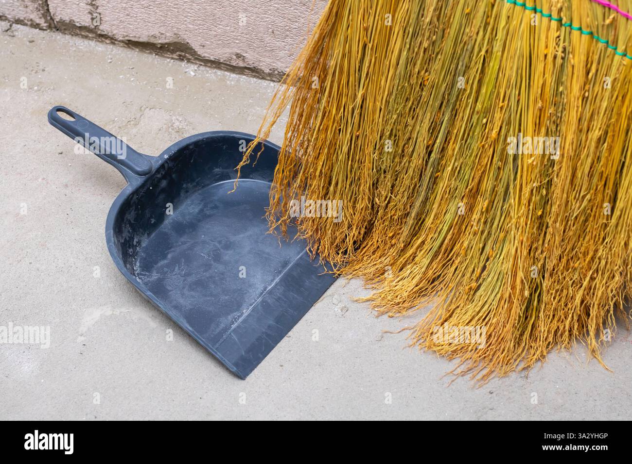A broom, alongside a black scoop, is positioned on the ground, ready ...