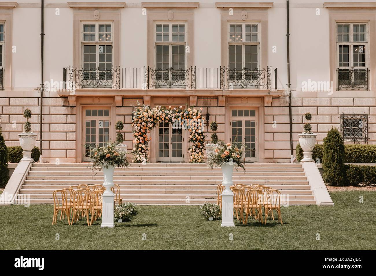 Elegant outdoor wedding setup with floral arch in front of a mansion ...