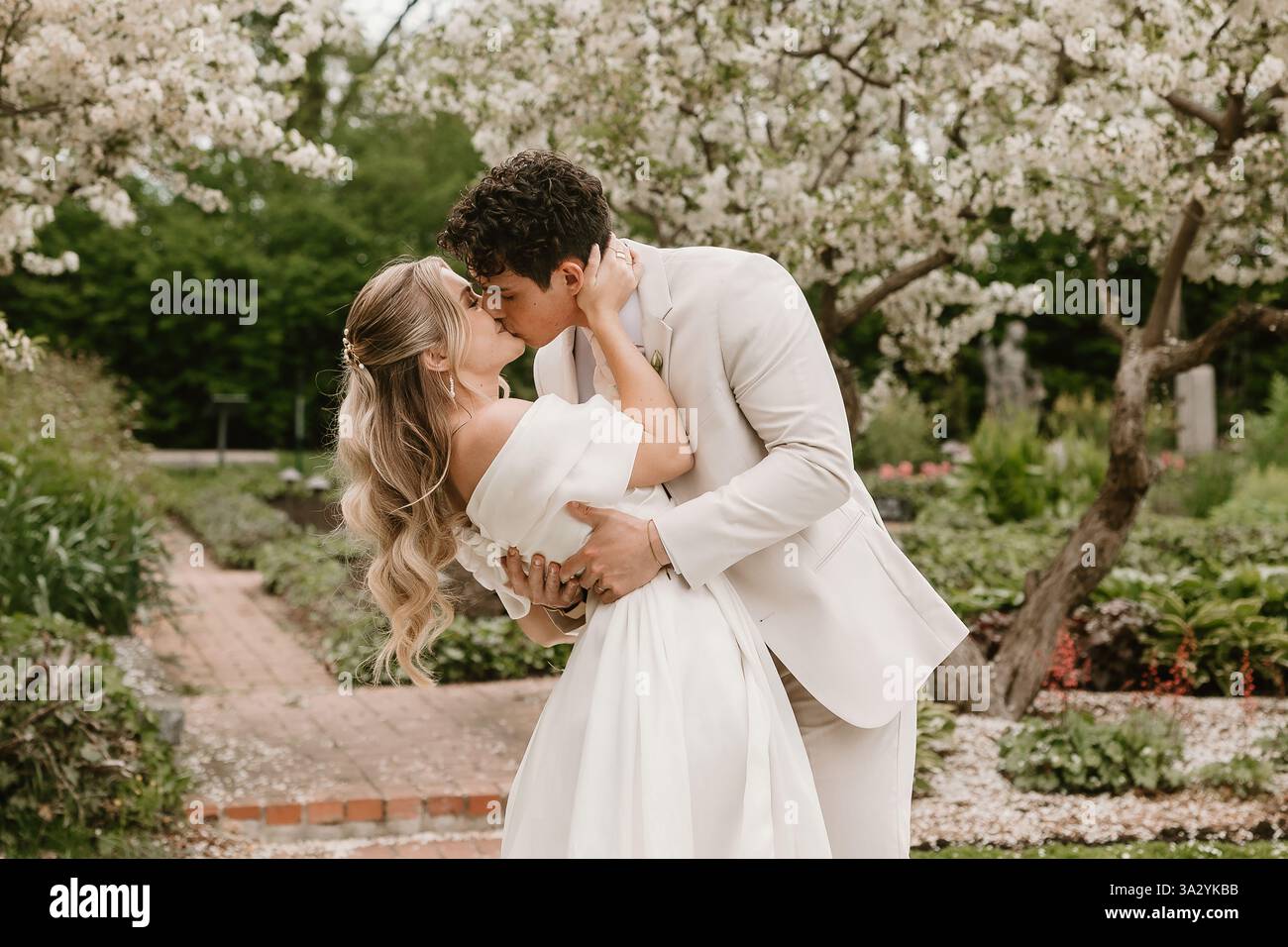 Bride and groom share a romantic kiss under blooming trees in a garden ...