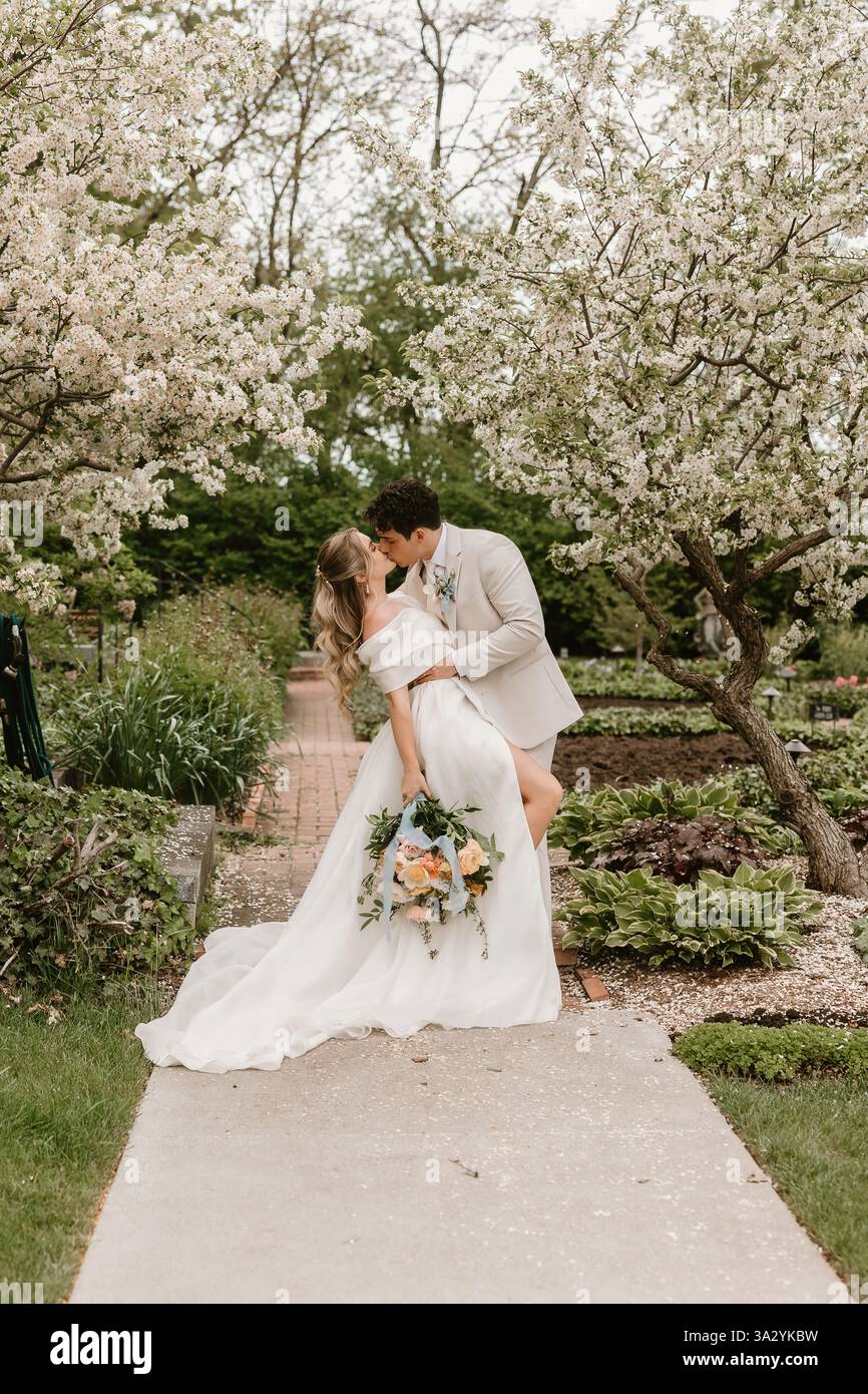 Bride and groom share a romantic kiss under blooming trees in a garden ...