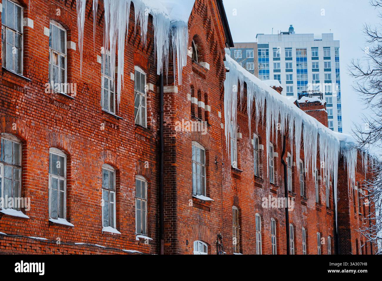 Sharp icicles dangling from snow-covered brick roof, framing weathered ...
