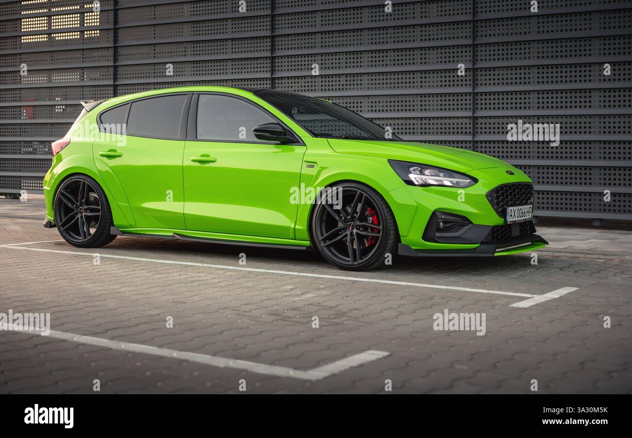 Lime green Ford Focus parked along the wall of grey warehouse at dusk ...