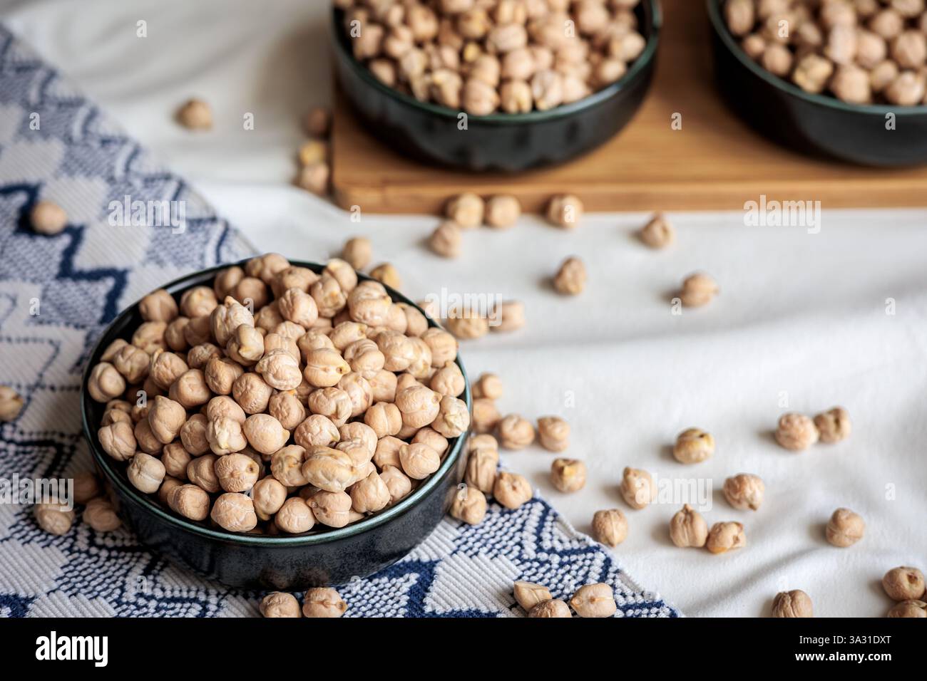 A composition of dried chickpeas in ceramic bowls on a soft fabric and ...