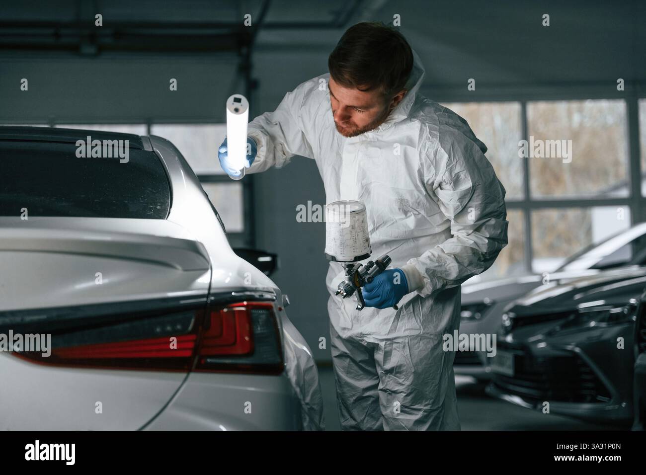 Rear part of automobile. Garage worker is holding lighting and checking ...
