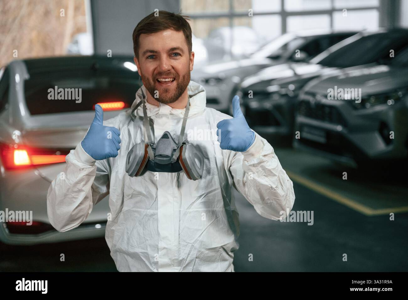 Standing in the garage with cars. Portrait of professional painter with ...