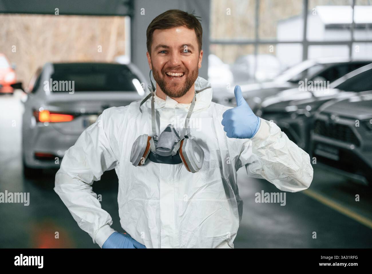Standing in the garage with cars. Portrait of professional painter with ...