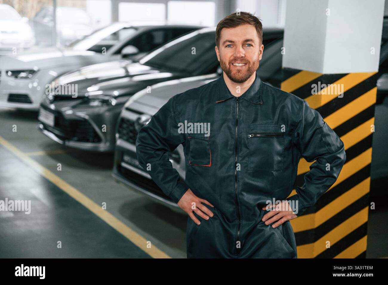 Repairman in uniform is standing in the garage with cars Stock Photo ...