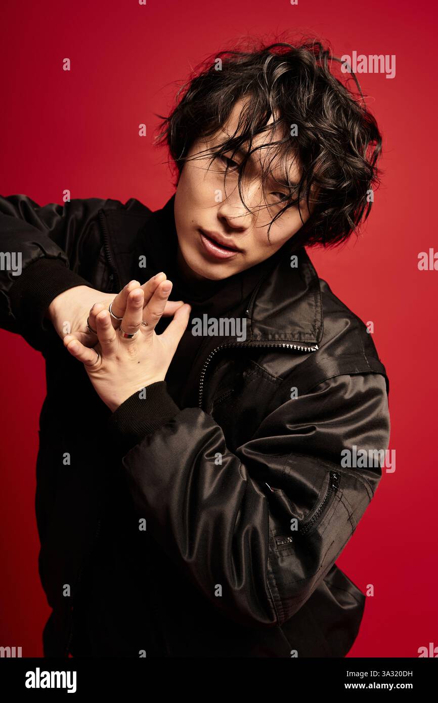 Young Asian man in black poses with hand gestures against a red ...