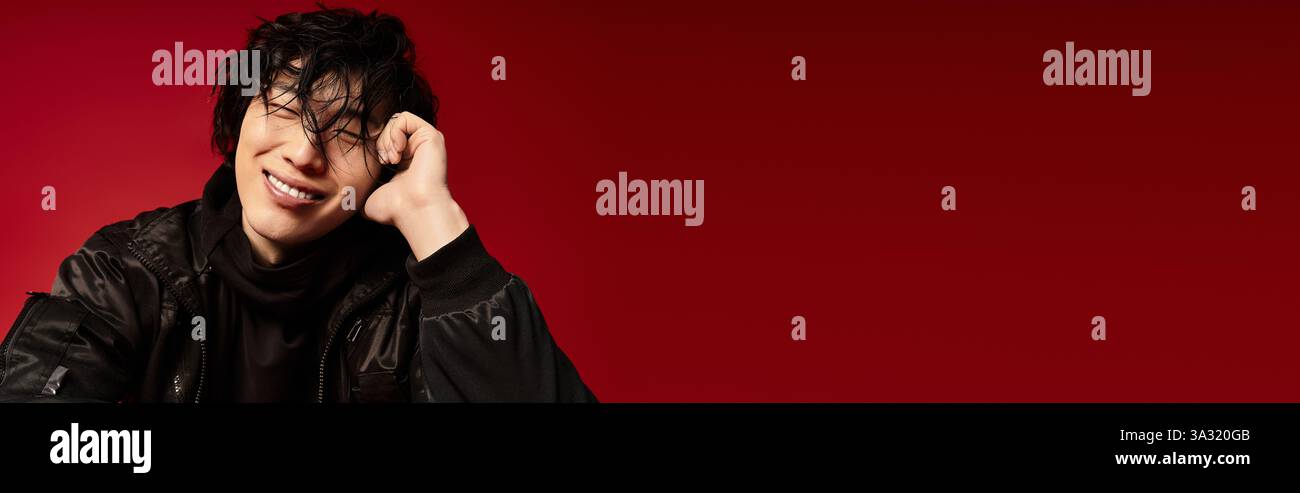 Young Asian model in black jacket smiles warmly in red-lit studio ...