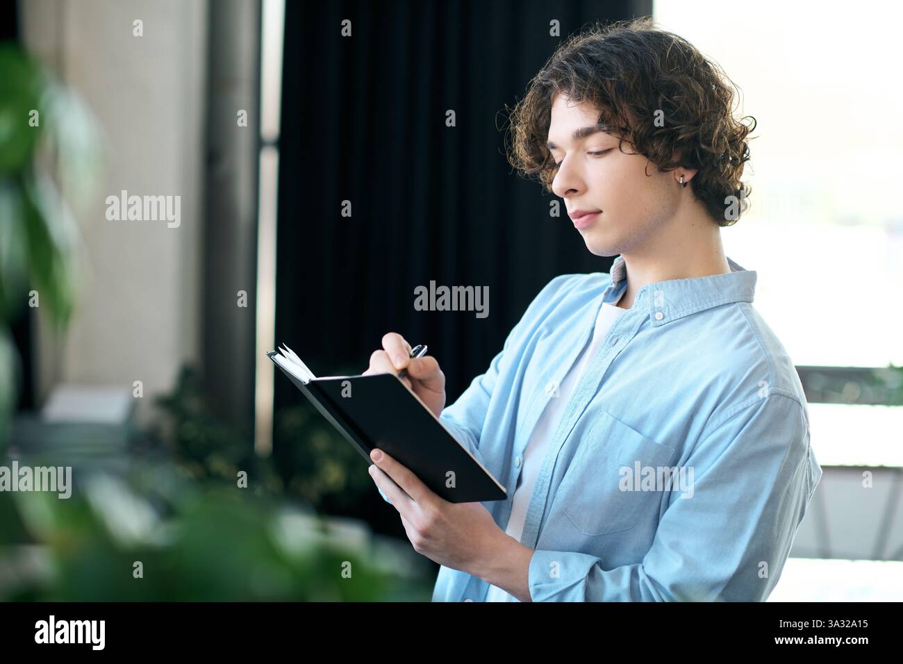 A young handsome man is intently jotting down notes in a notebook at ...