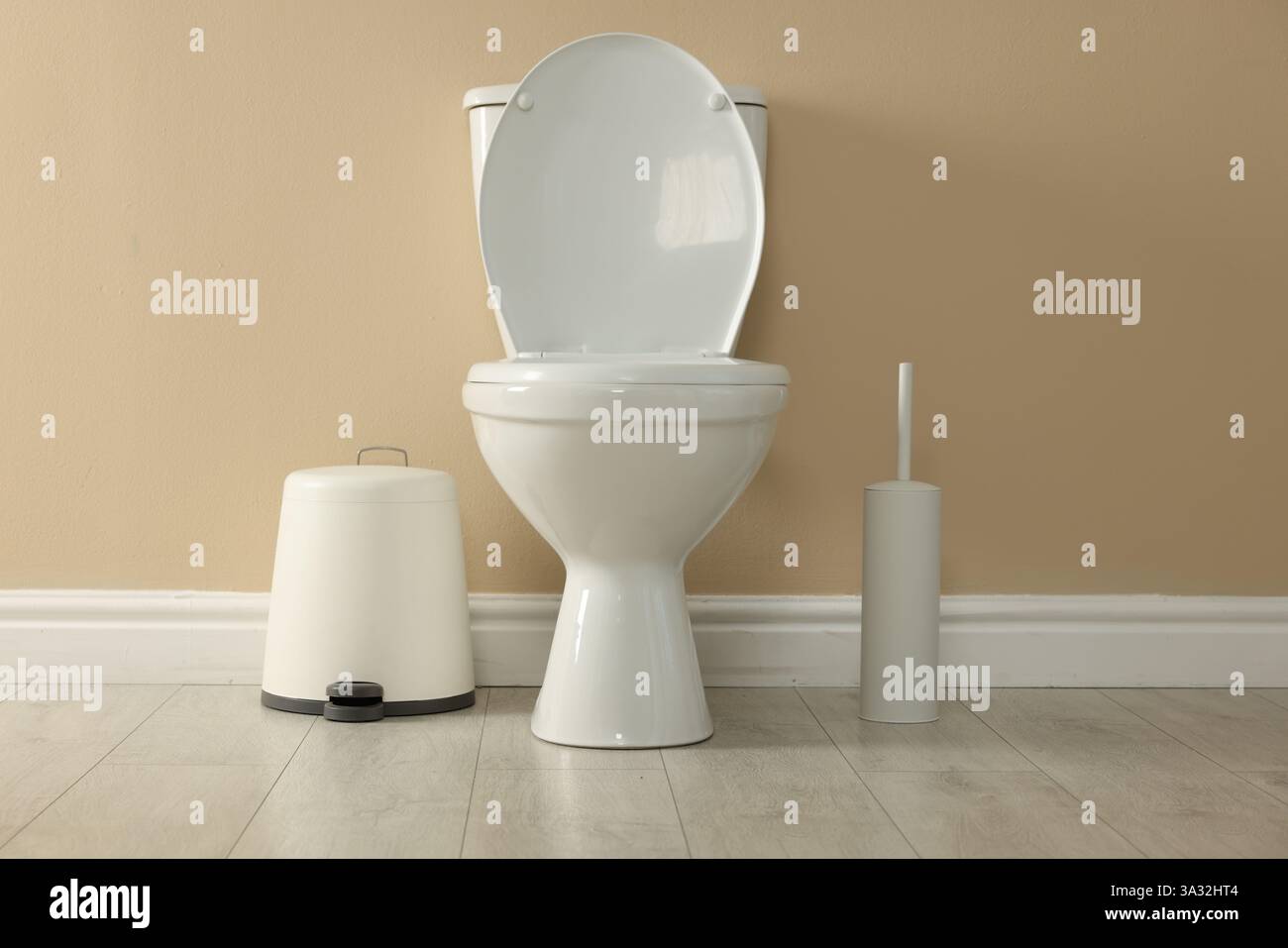 Toilet bowl, brush and trash bin near beige wall in restroom Stock ...