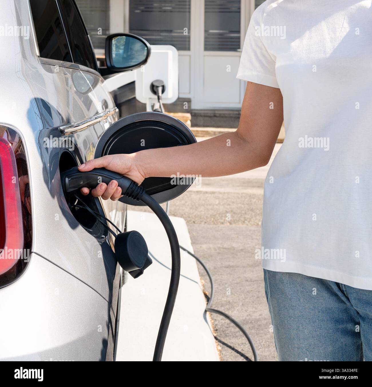 Female driver charging her electric car at an EV charging station on a ...