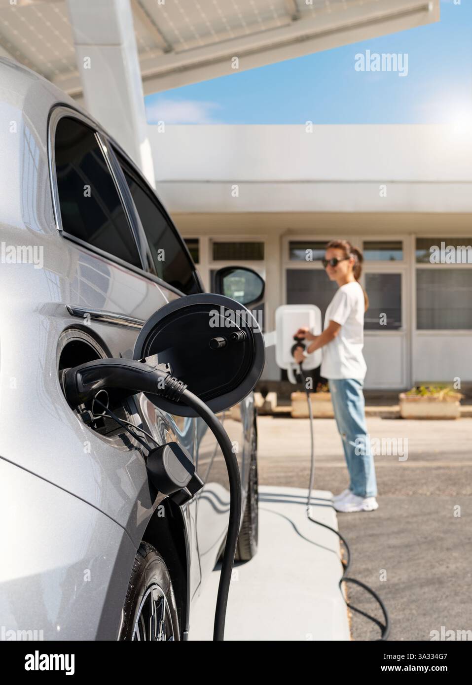 Female driver charging her electric car at an EV charging station on a ...