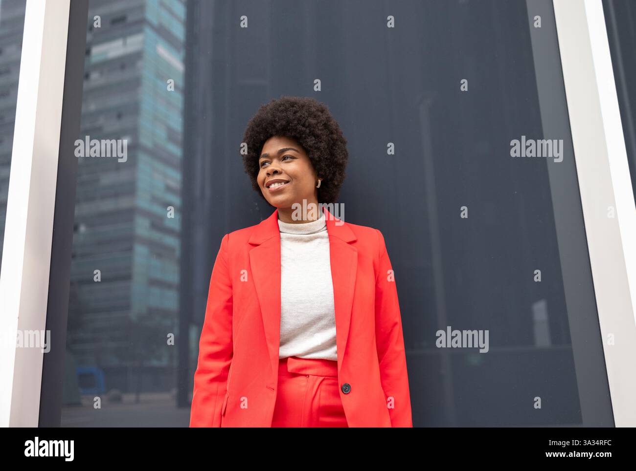 A woman in a bright red suit stands confidently against a modern urban ...