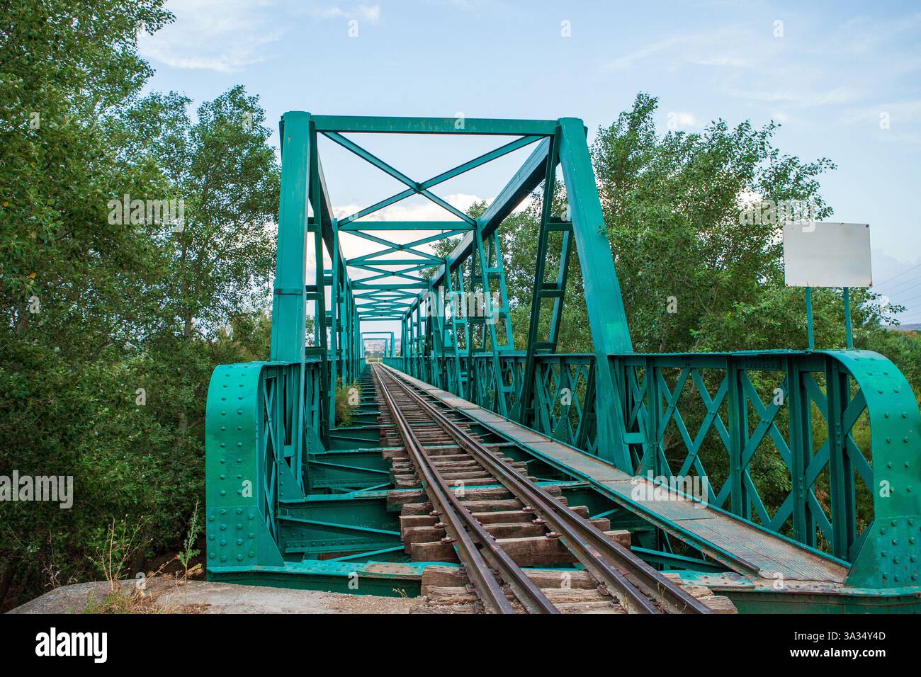 An aged green railroad bridge with rust and weathering stretches over ...
