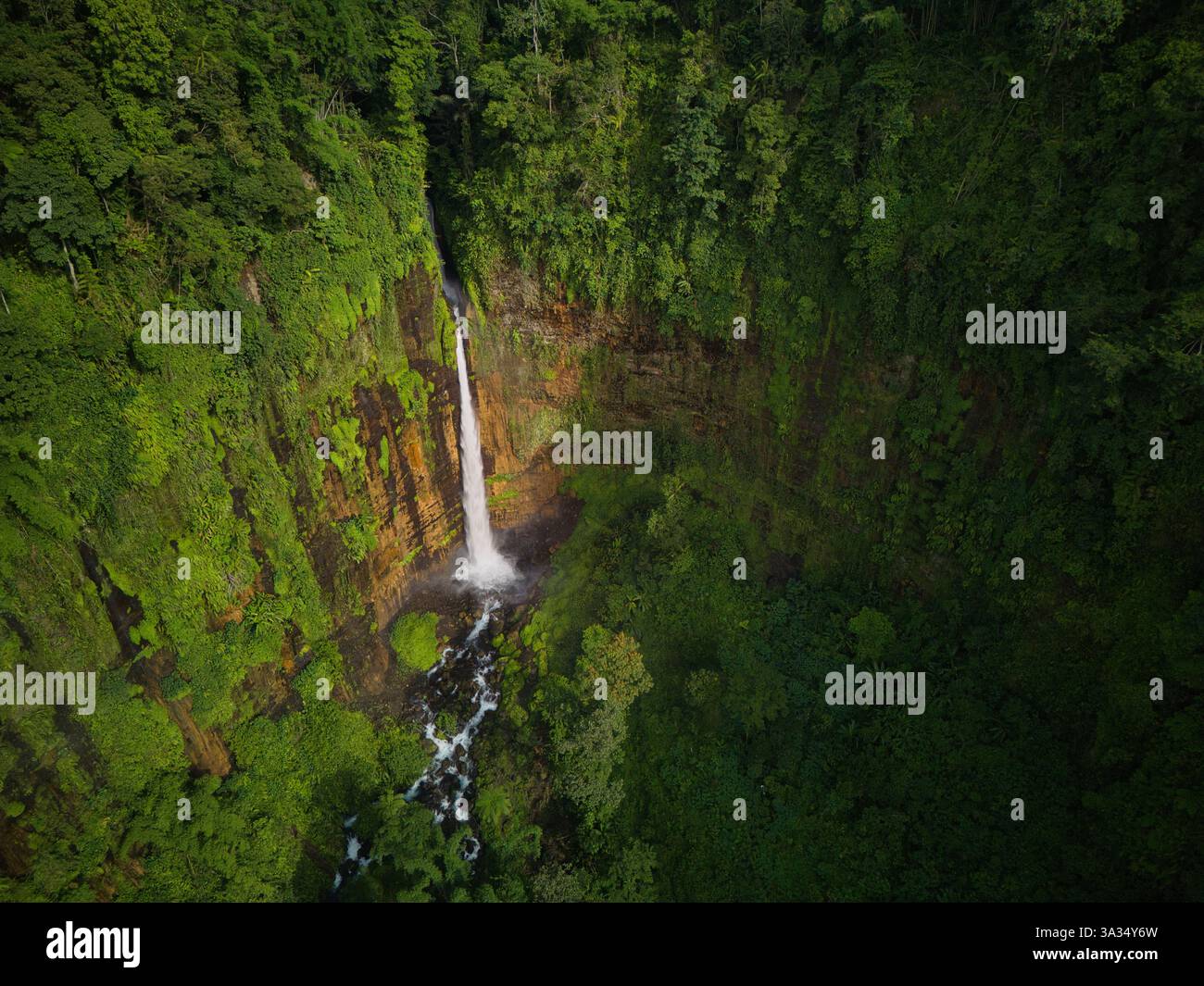 Aerial shot capturing the majestic Kaspa Biru Waterfall descending into ...