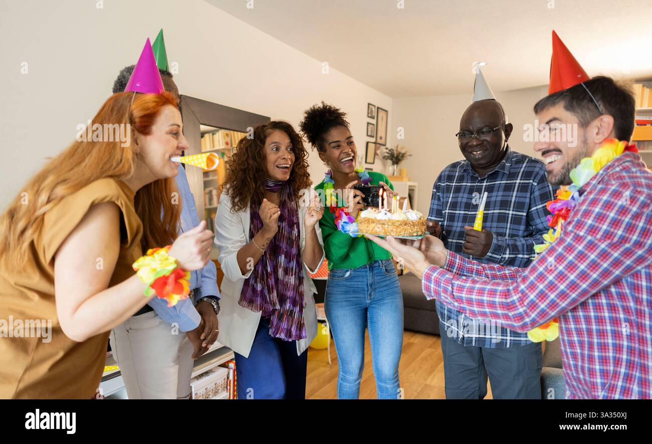 A joyful group of people celebrating a birthday indoors. They are ...