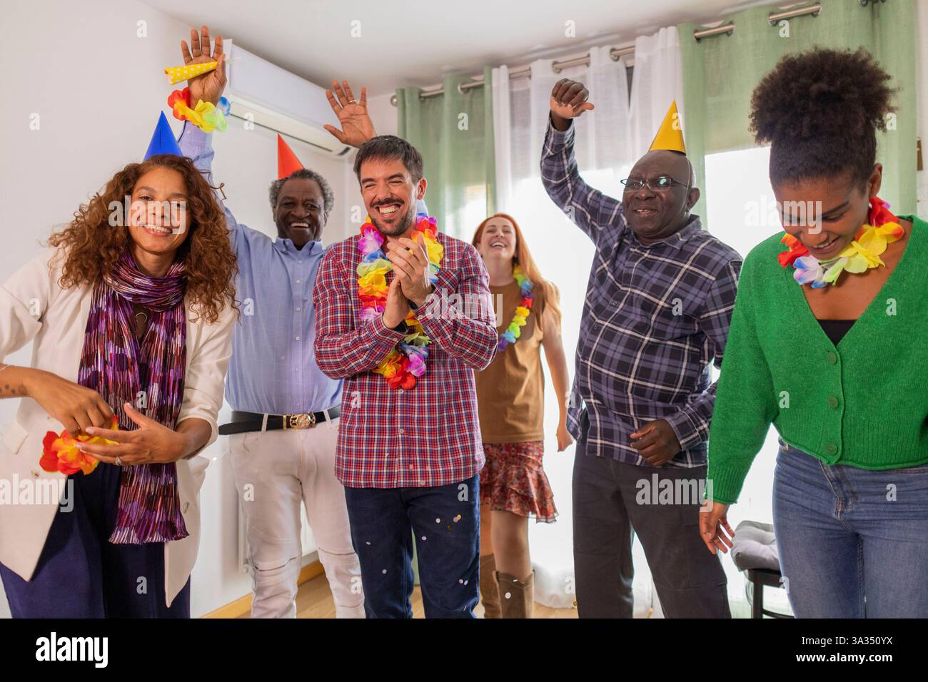 A group of six adults joyfully celebrate a birthday indoors, wearing ...