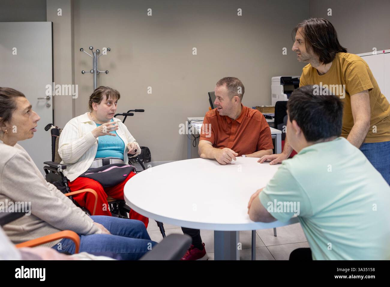 People gather around a table in a supportive day center. They engage in discussion, highlighting ...