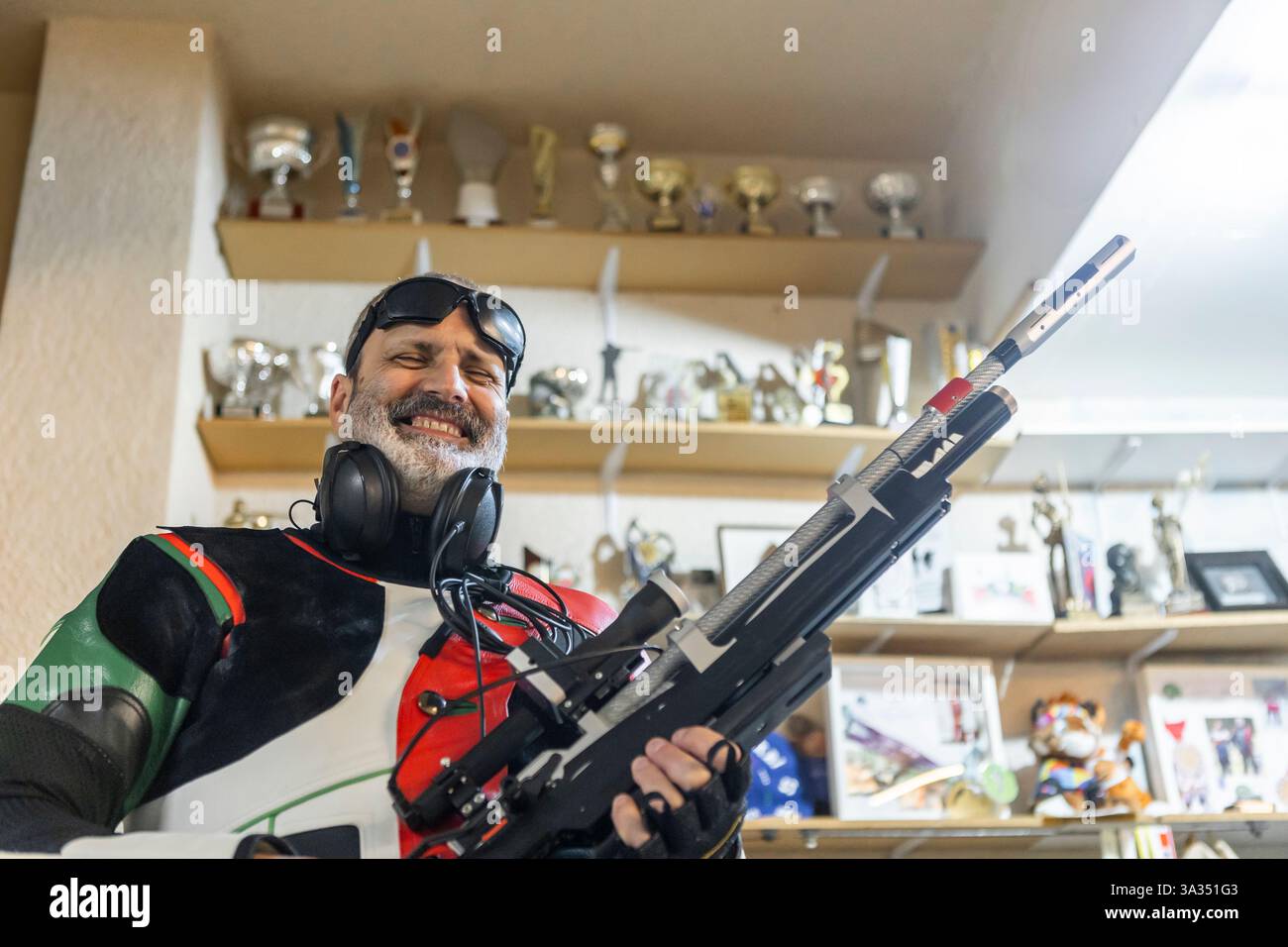 Blind athlete proudly holds a rifle, surrounded by numerous trophies ...