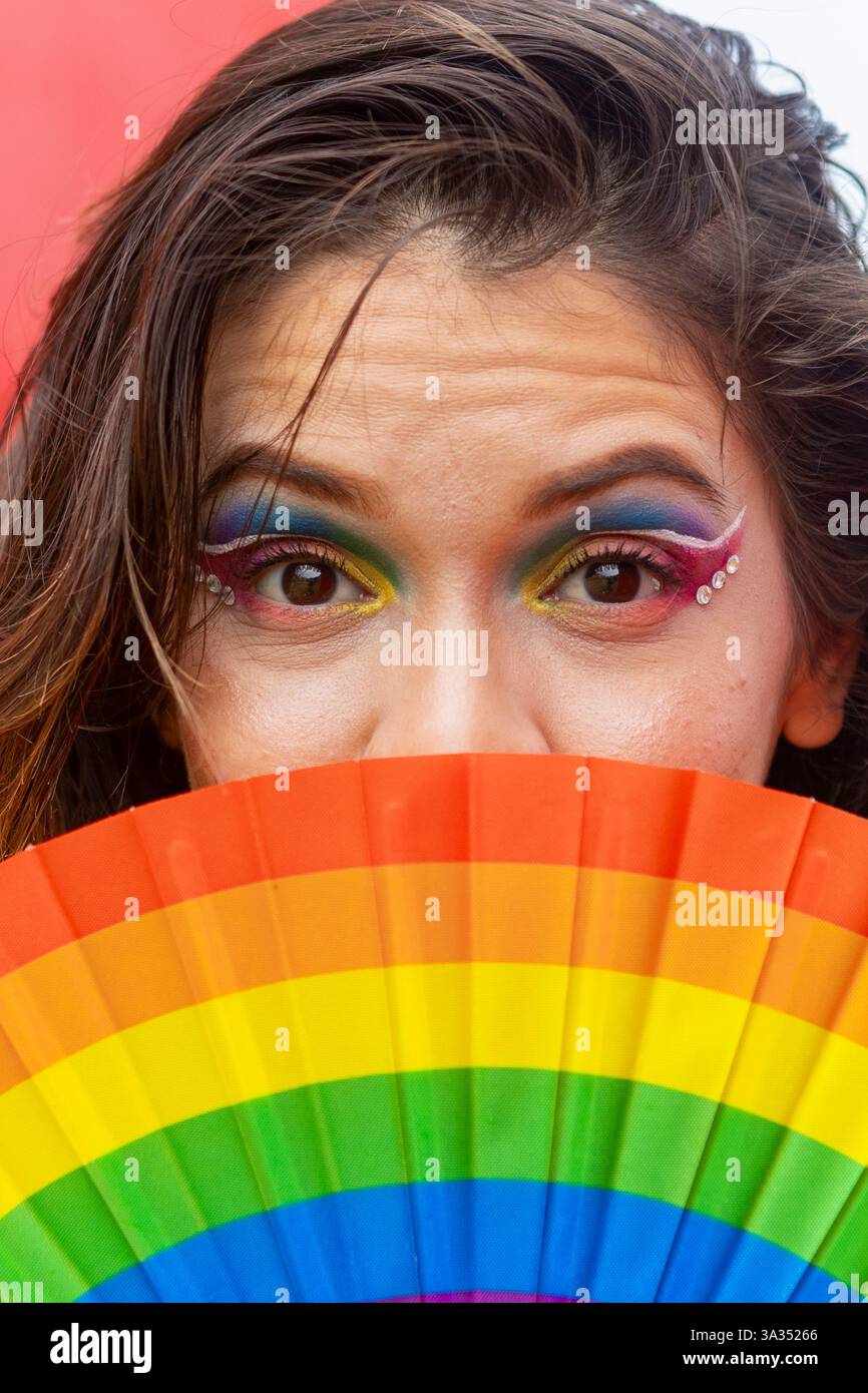 Close-up of a woman with vibrant rainbow makeup and jewels, holding a ...