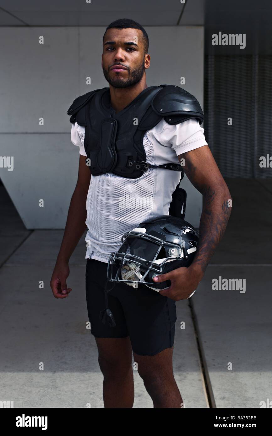 A focused football player stands with his helmet, dressed in shoulder ...