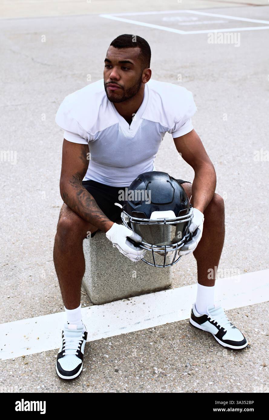 An american football player in a white jersey sits on a bench holding ...