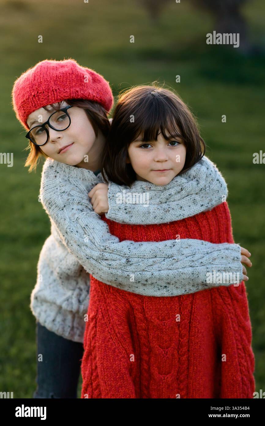 A boy and girl, siblings, warmly embrace in an autumn park setting ...