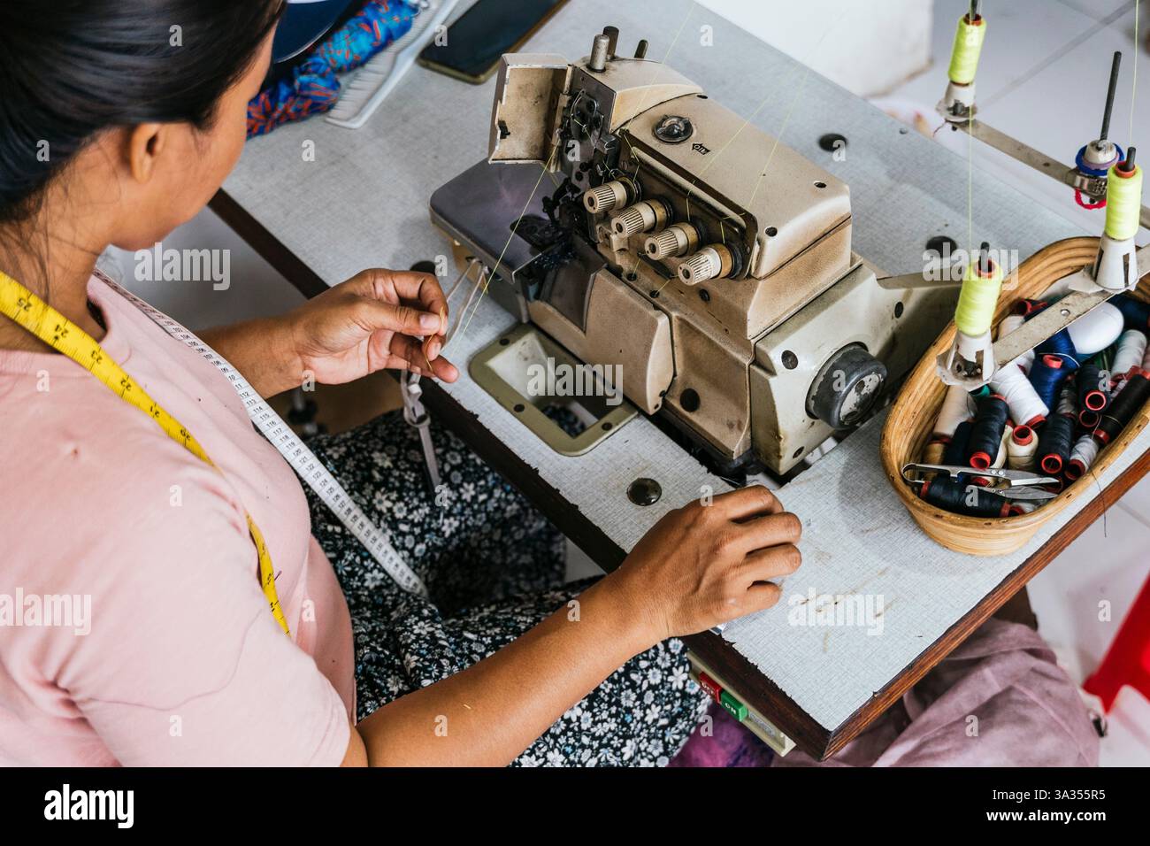 A asian seamstress works at a sewing machine, surrounded by threads and ...