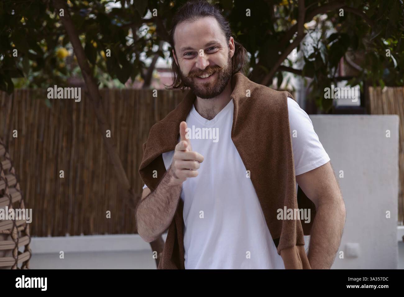 A man stands outside in daylight, smiling and pointing playfully at the ...
