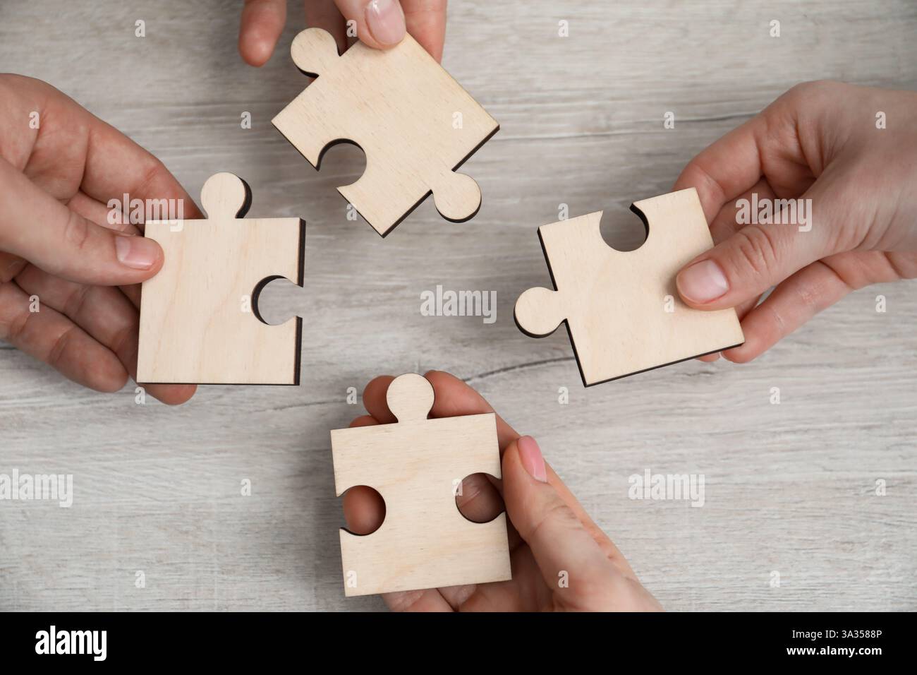Teamwork. Group of people putting puzzle pieces together at wooden table, top view Stock Photo ...