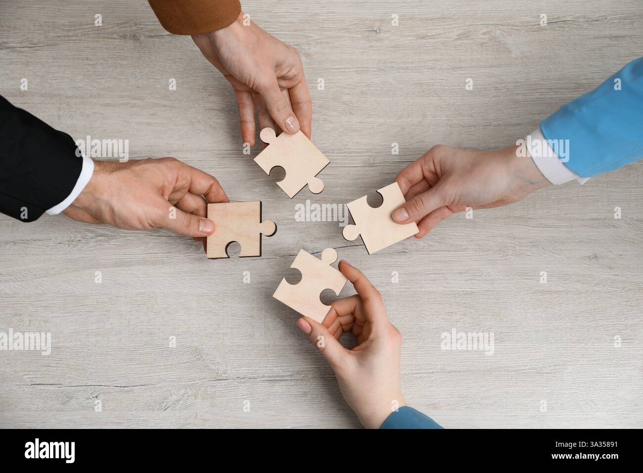 Teamwork. Group of people putting puzzle pieces together at wooden table, top view Stock Photo ...