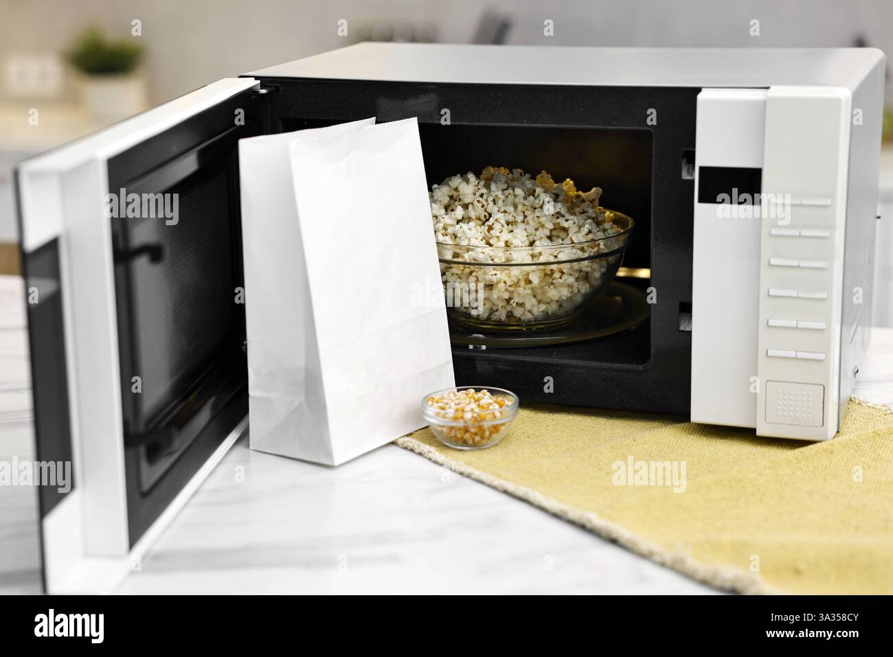 Open microwave oven with bowl of popcorn, paper bag and kernels on ...