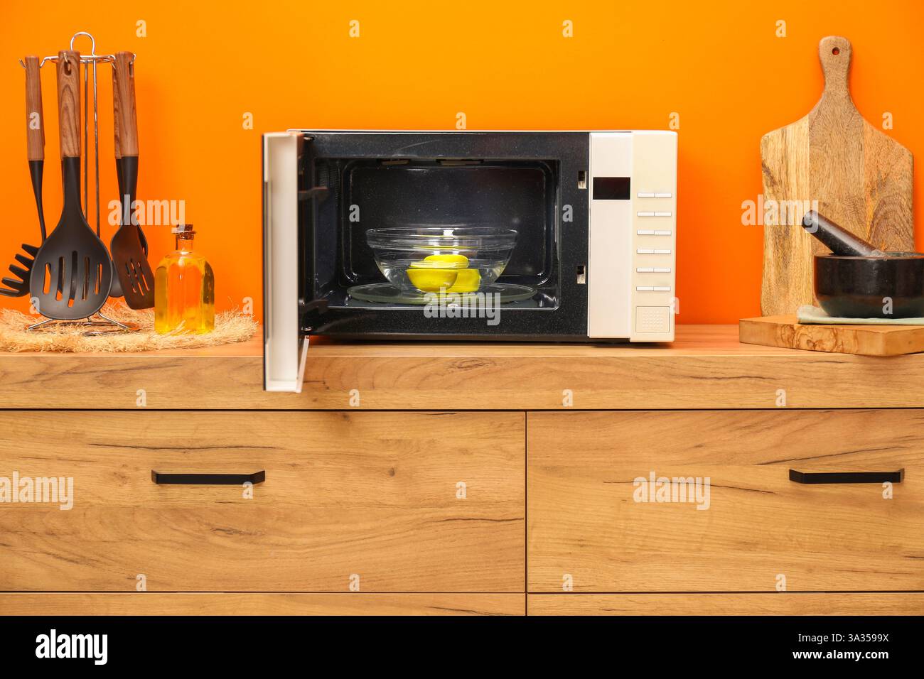 Open microwave oven with bowl of water and lemons on wooden cabinet ...