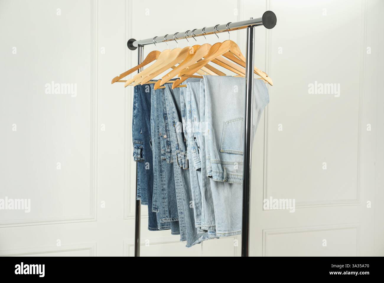 Many stylish jeans hanging from rack near white wall Stock Photo - Alamy