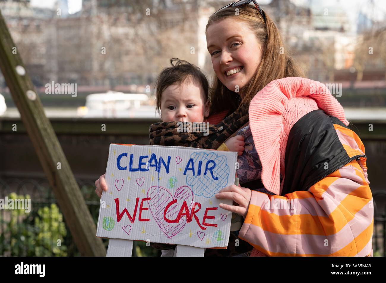 London, UK. 14 March, 2025. A mother and toddler hold a placard saying ...