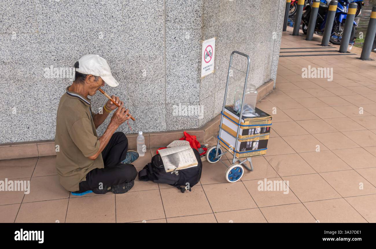 a street musician sitting on the ground playing a flute, busker, Kuala ...